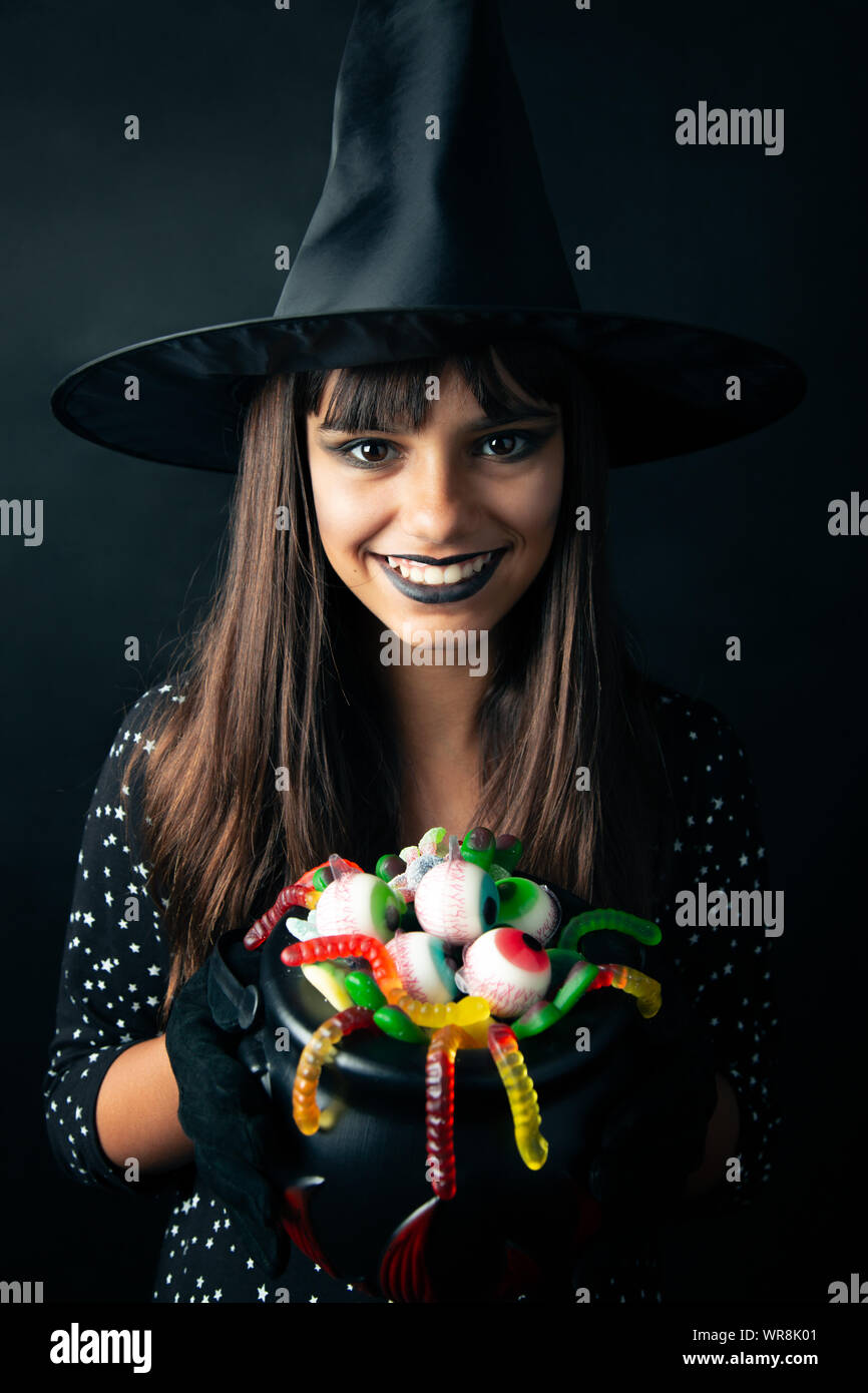 Happy young Halloween witch holding a cauldron full of candies with ...