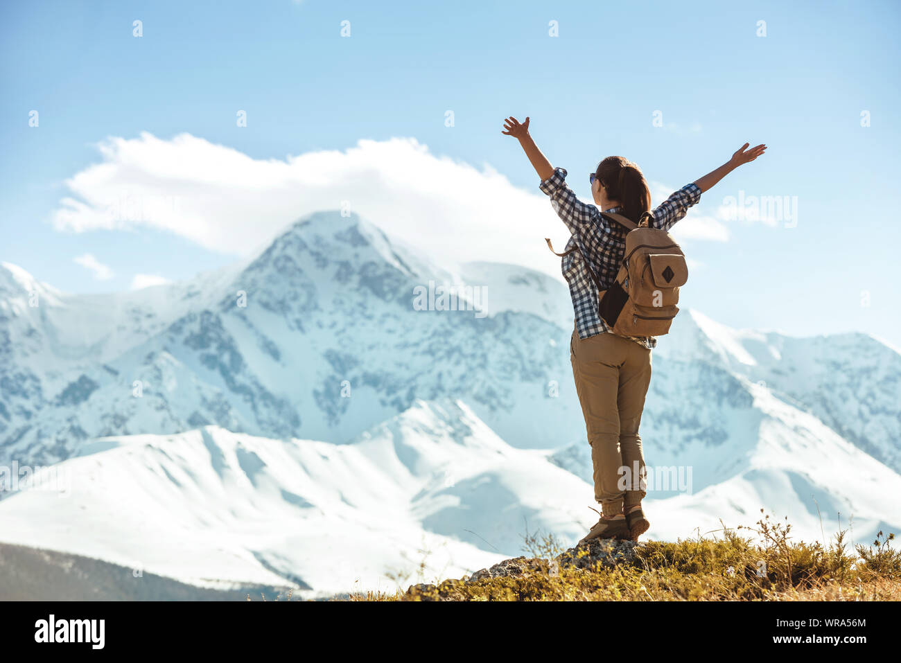 Happy lady hiker is standing with raised arms against mountains with ...