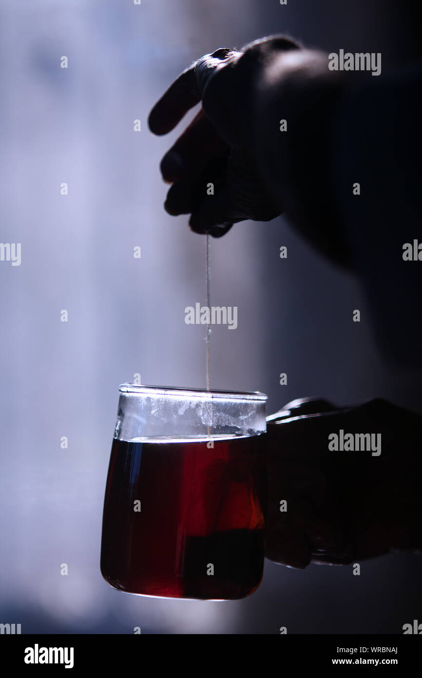 Close up of a man's hand holding a teabag dipped into hot water in ...