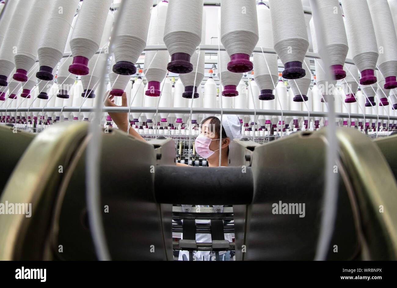 A female Chinese worker checks spindles of yarn on a spinning machine ...