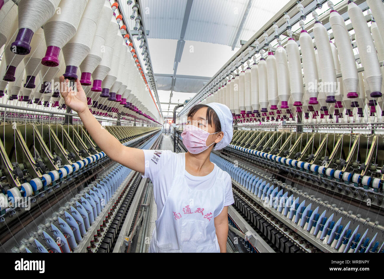 A female Chinese worker checks spindles of yarn on a spinning machine ...