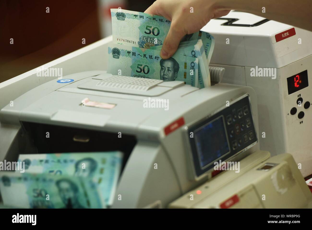 A Chinese employee counts 50-yuan banknotes of the 2019 edition of the ...