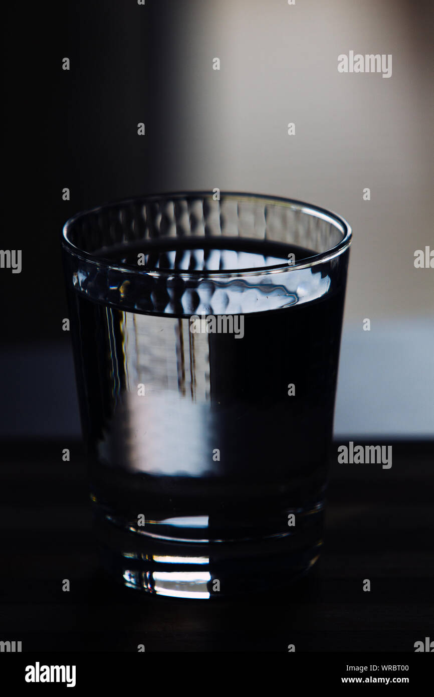 High angle close up of a glass of water left in dark. Still water in ...