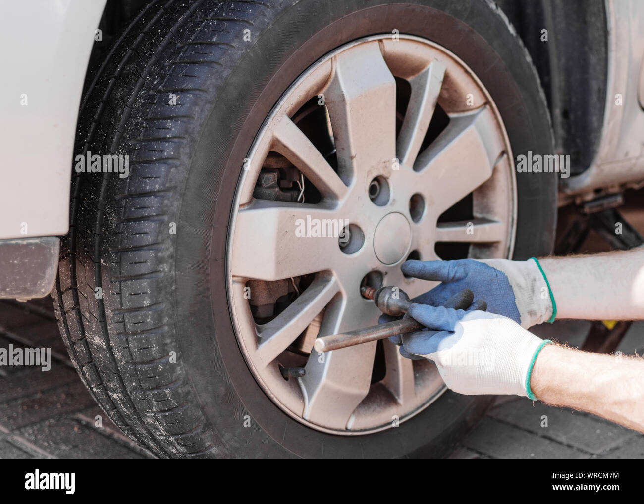 Mechanic changing wheel on car with a wrench outdoor in a sunny day ...