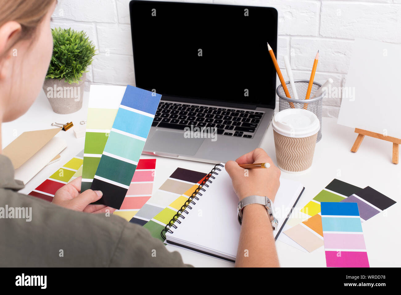 Woman writing numbers of colors in notebook on office table with laptop ...