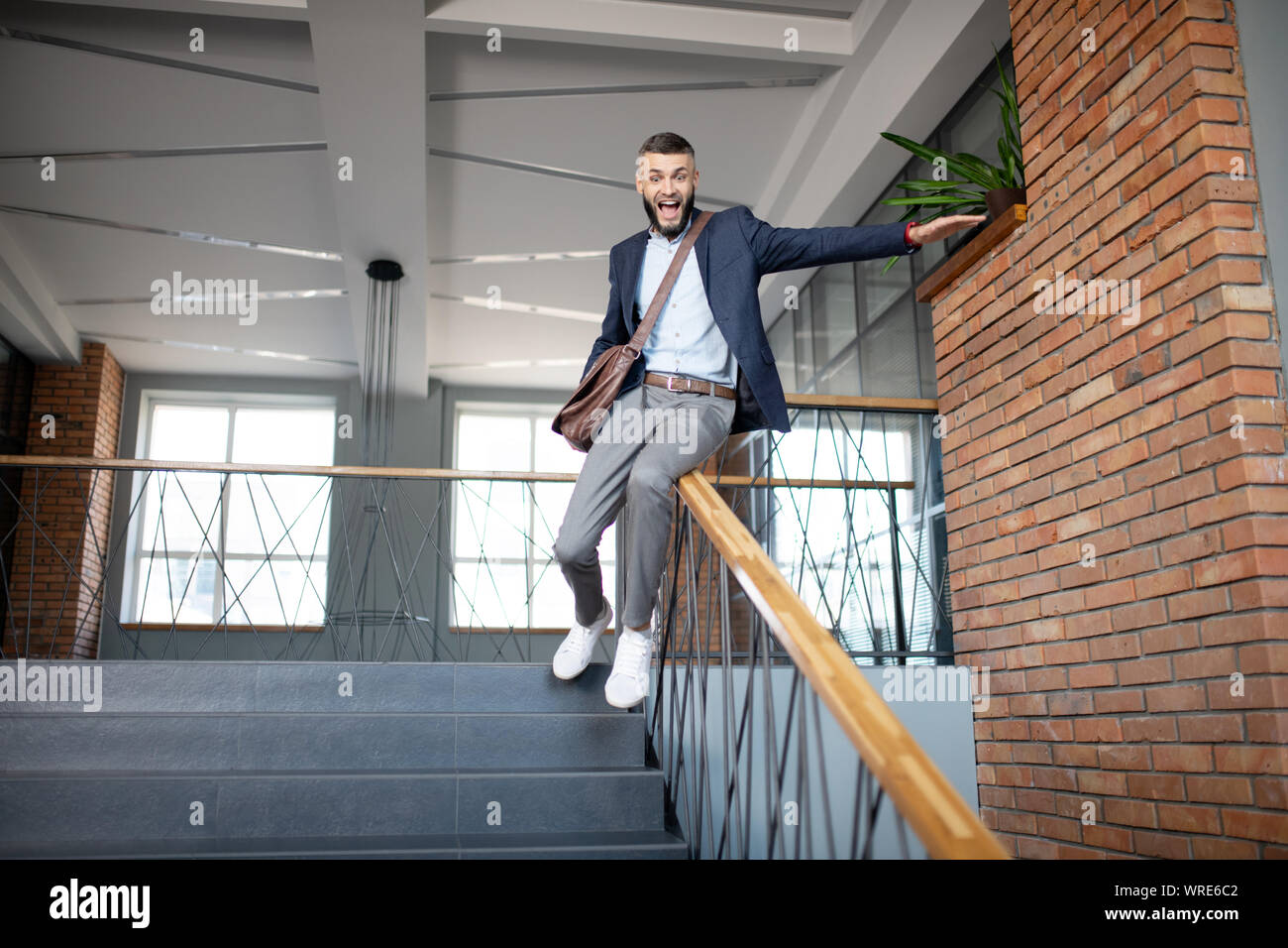 Cheerful man having fun while sliding on the banister Stock Photo - Alamy