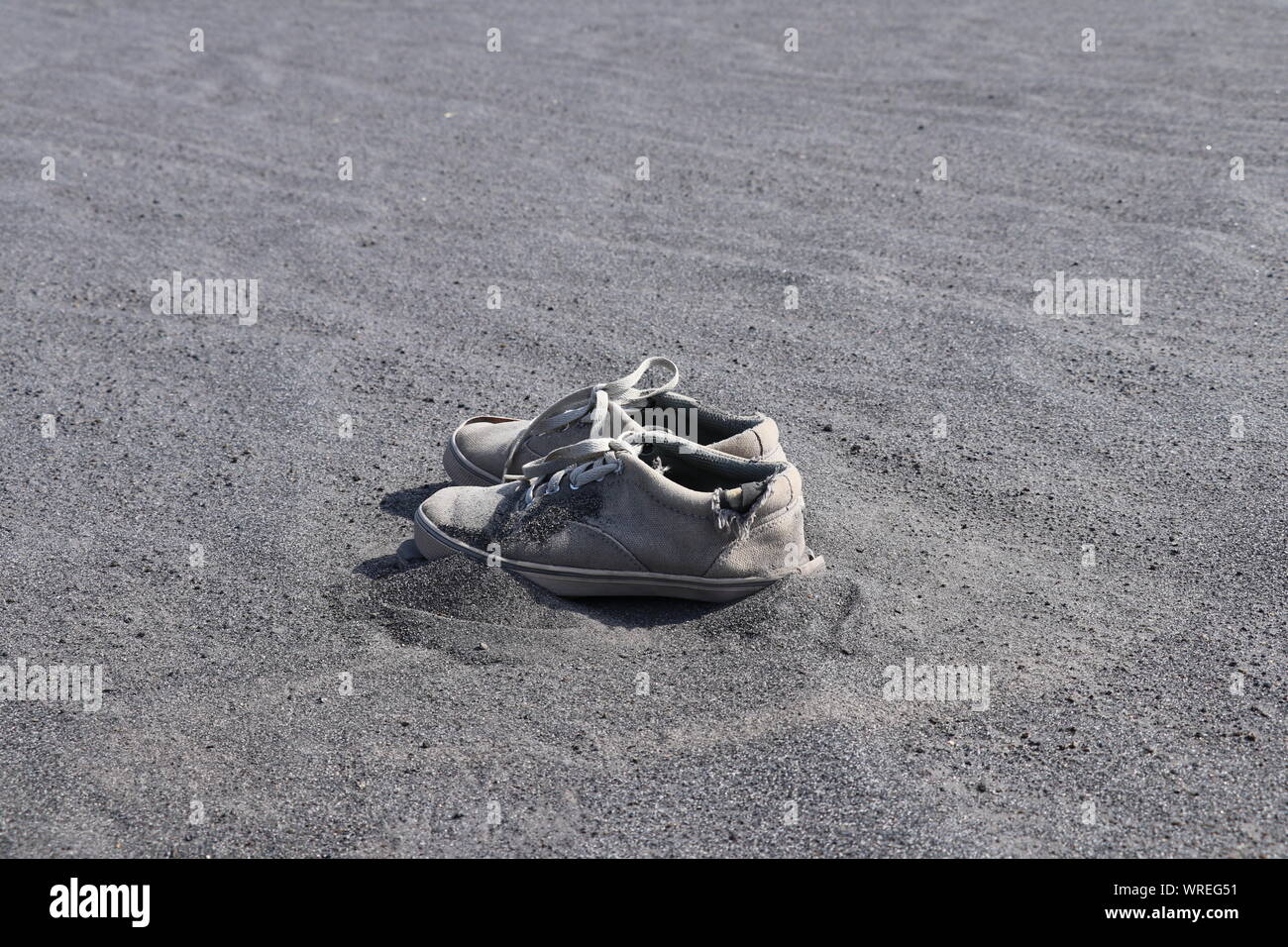 Old torn white sneakers on black volcanic sand. A pair of tie shoes ...