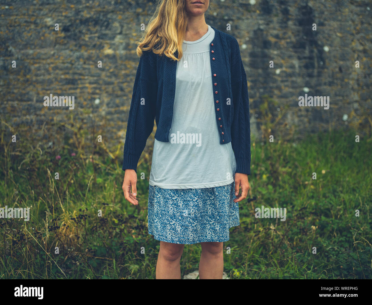 A young woman is standing by a wall in the countryside Stock Photo - Alamy