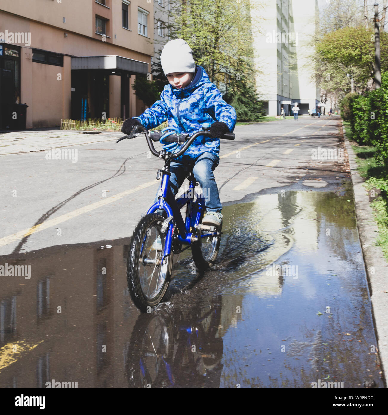 Boy child riding his bike across puddle in the street Stock Photo - Alamy