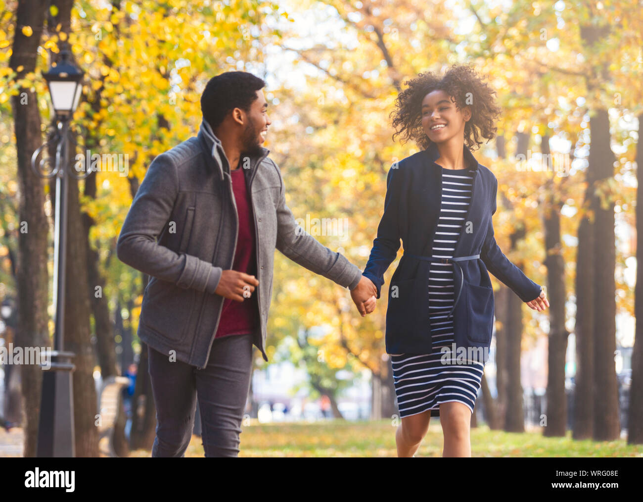 Happy black couple running over golden park Stock Photo - Alamy