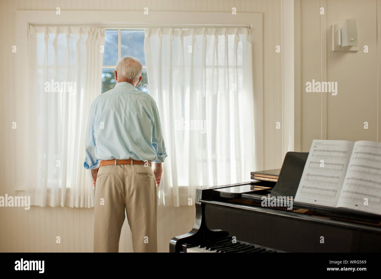 Senior man looking out the window next to a piano Stock Photo - Alamy