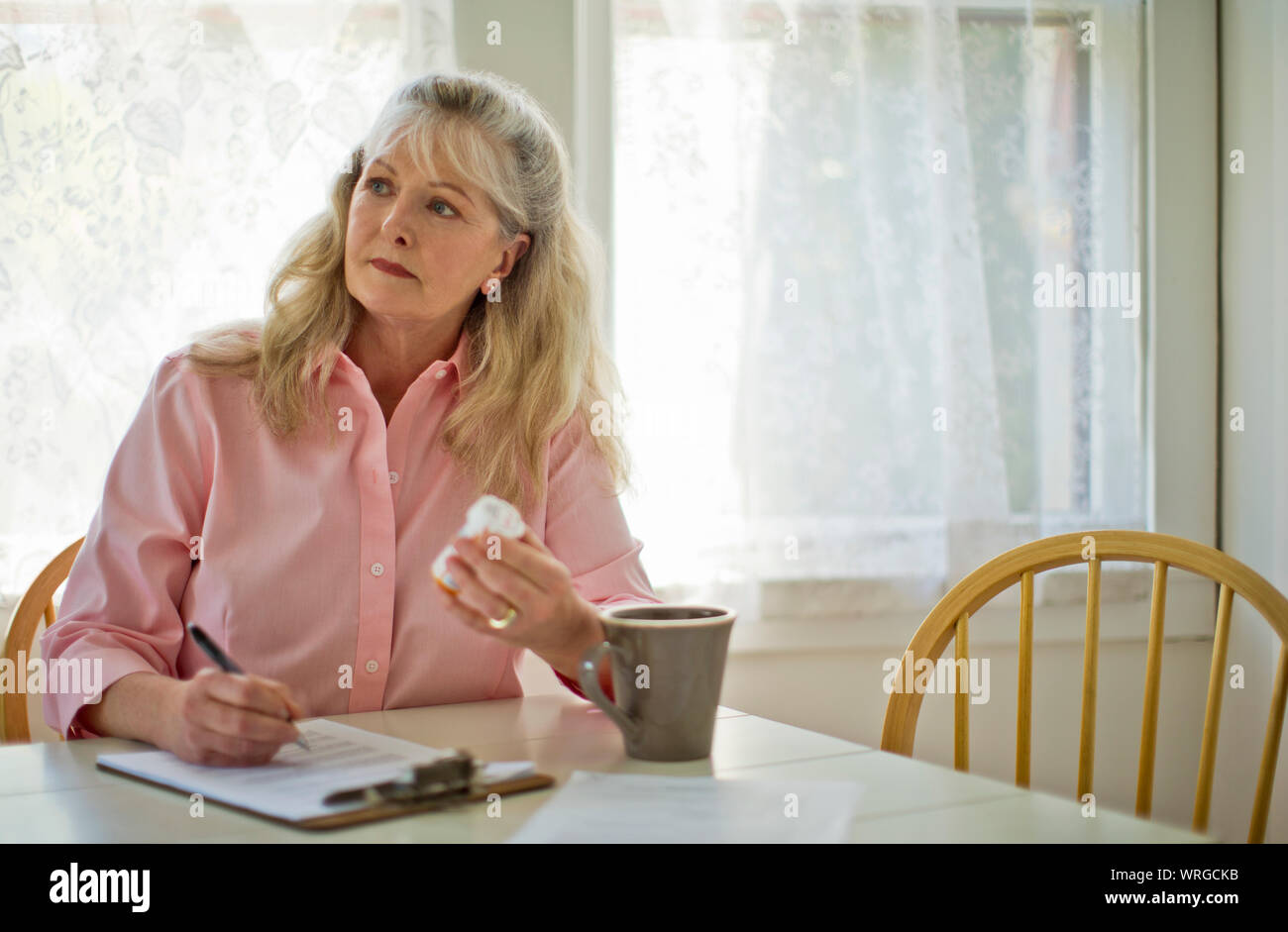 Senior woman taking notes while holding a medicine bottle Stock Photo ...