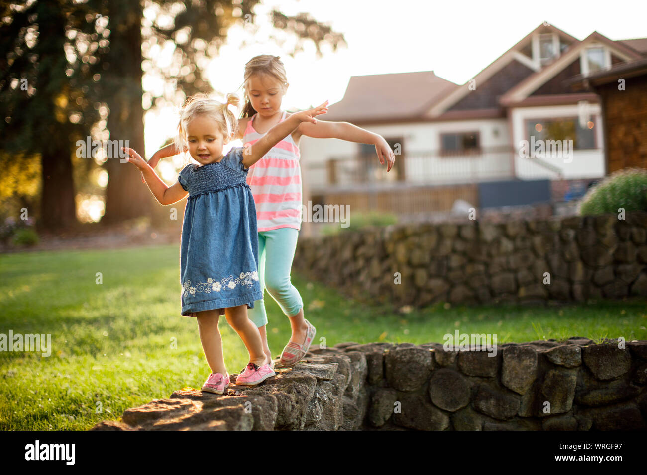 Two sisters playfully balancing on a stone wall Stock Photo - Alamy