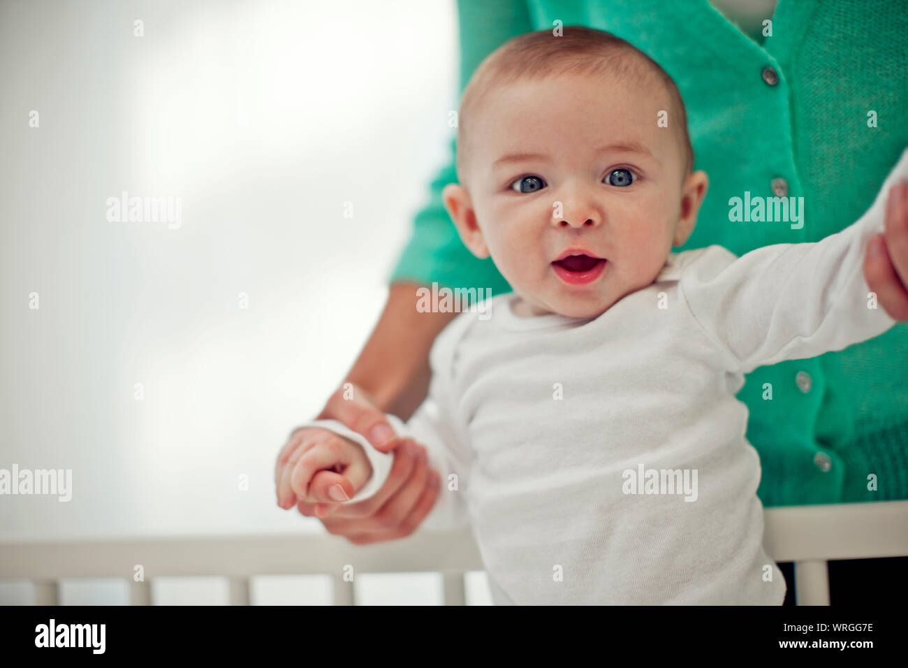 Cute smiling baby boy is supported by his mother's hands as she helps ...
