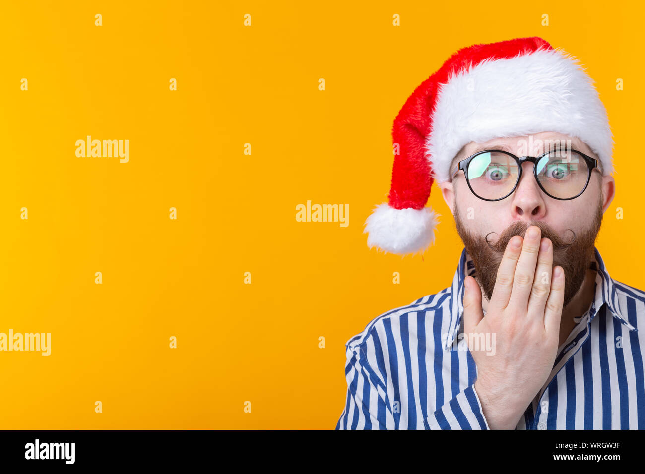 Surprised young man Santa Claus startledly closes his mouth while ...