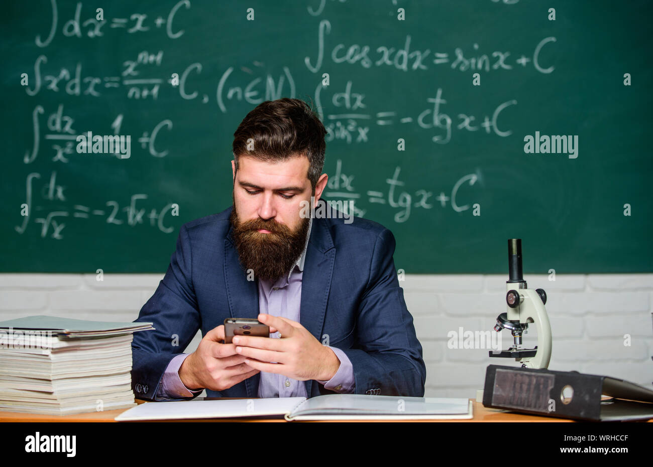 School teacher hold mobile phone chalkboard background. Teacher bearded ...