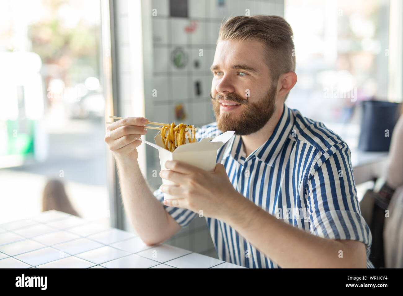 Positive young stylish guy eating chinese noodles in a cafe during a ...