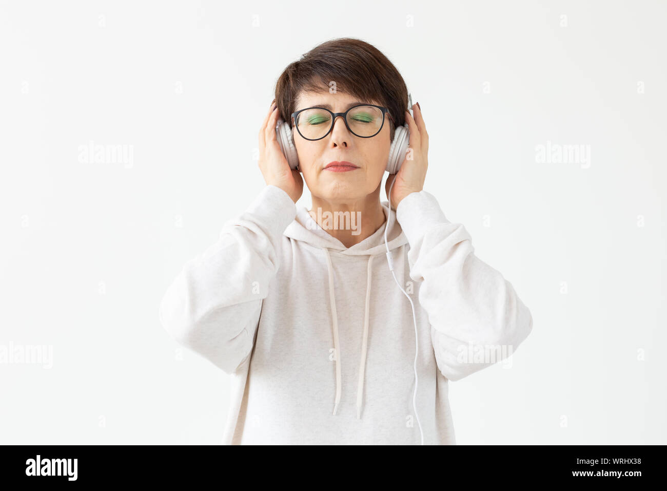 Cute positive middle-aged woman in sweater and glasses is listening to ...