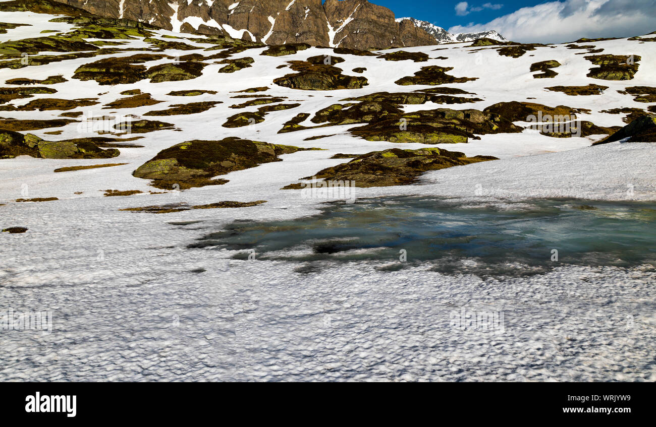 A small frozen lake in the Alps in early spring on a sunny day. Snow ...