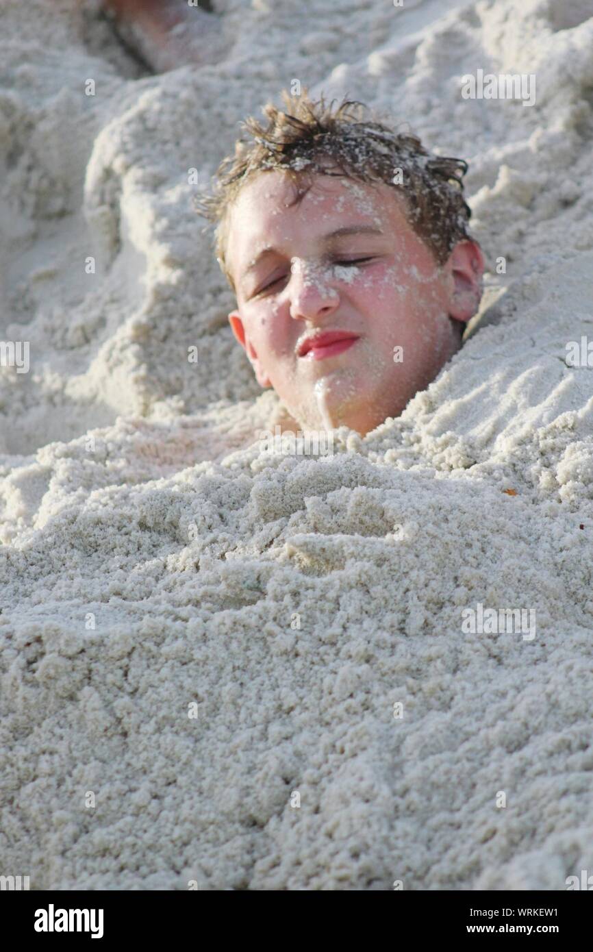 Teenage Boy Buried In Sand Stock Photo - Alamy
