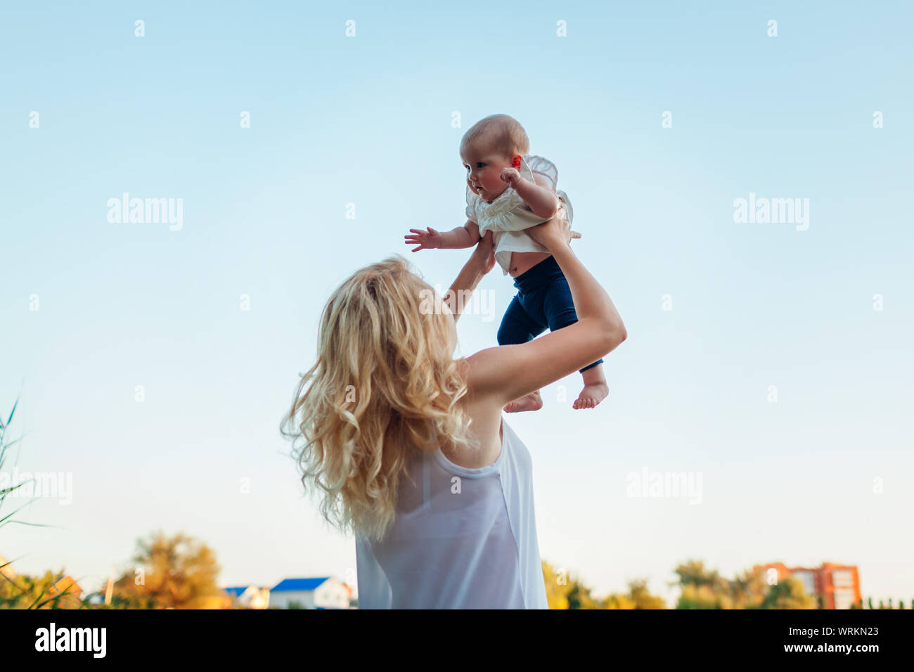 Young mother walking by summer river with baby girl. Woman lifting kid ...