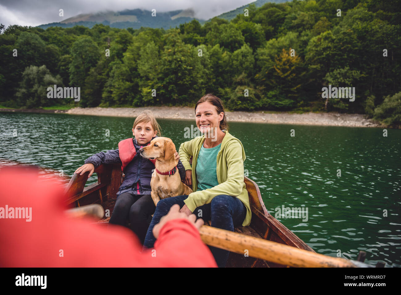 Family with small yellow dog rowing on the mountain lake in a boat ...