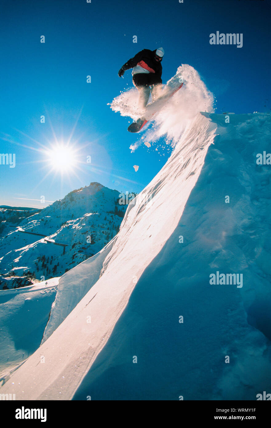 Snowboarder jumping off a cliff off piste, backlit by the sun on a ...