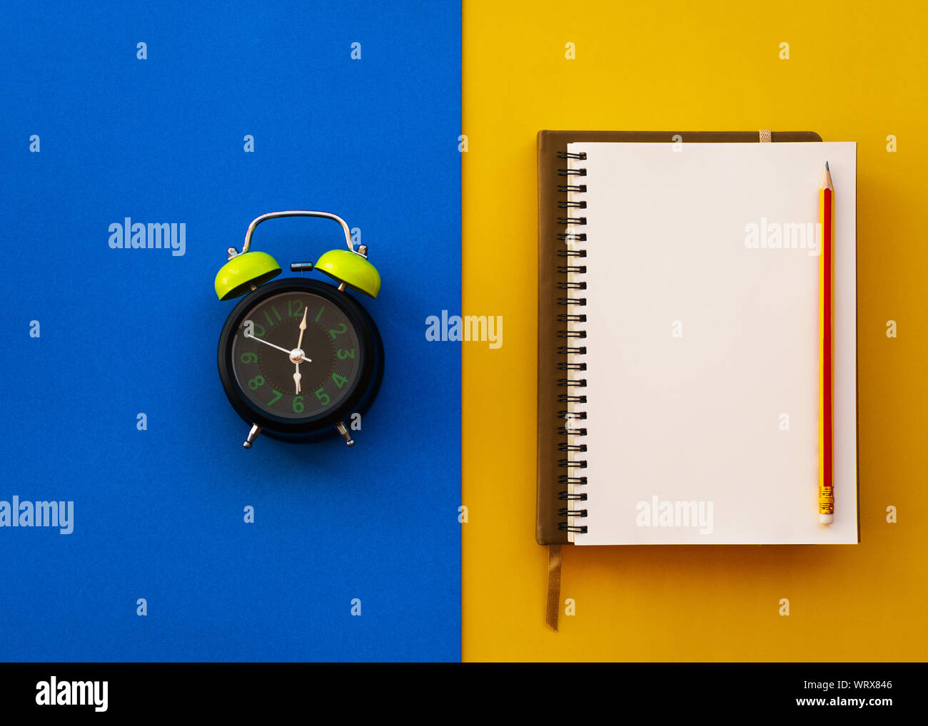 Blank white notepad with pencil and alarm clock isolated on two tone ...