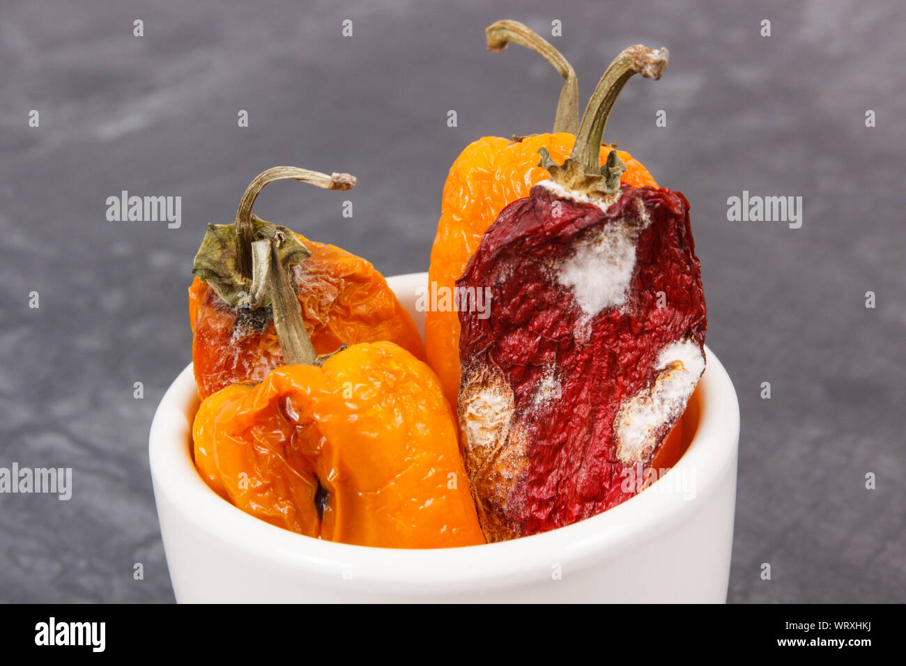 Old wrinkled moldy peppers in white bowl on dark background, concept of ...