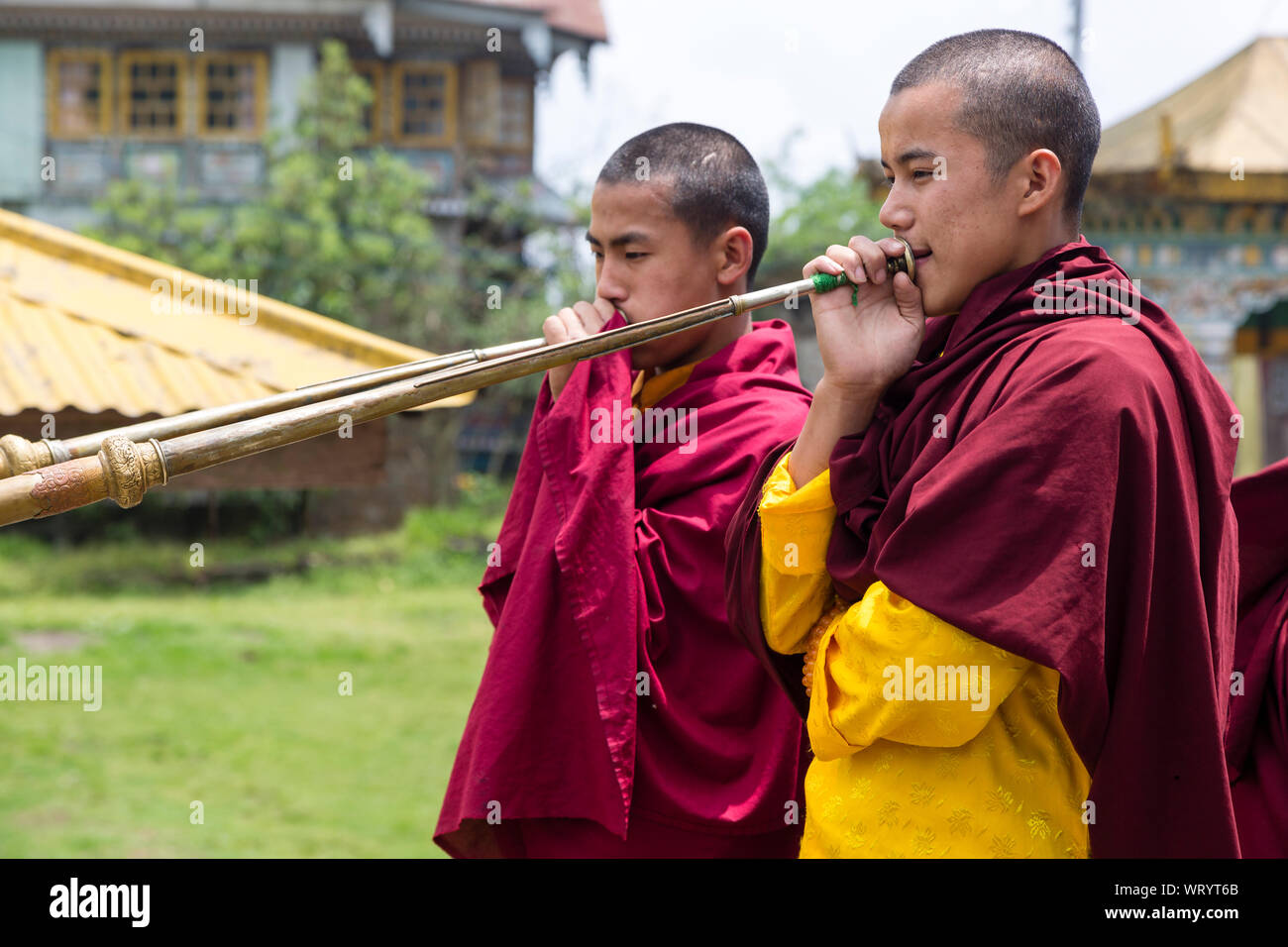Two young monks play on a long trumpet musical instrument at the ...