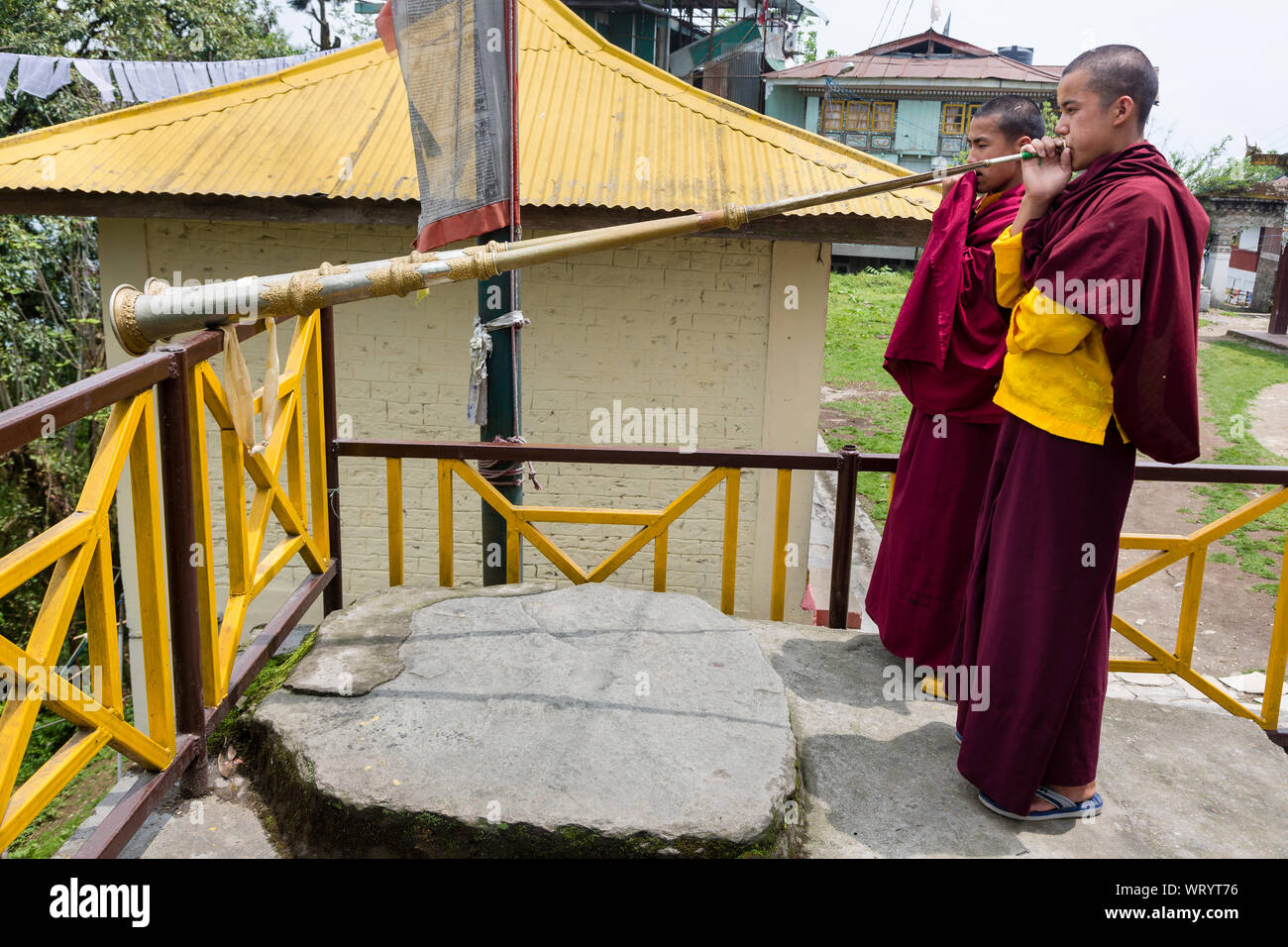 Two young monks play on a long trumpet musical instrument at the ...