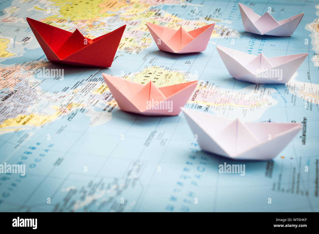 Paper boats following a red leader boat on world map. Concept for ...