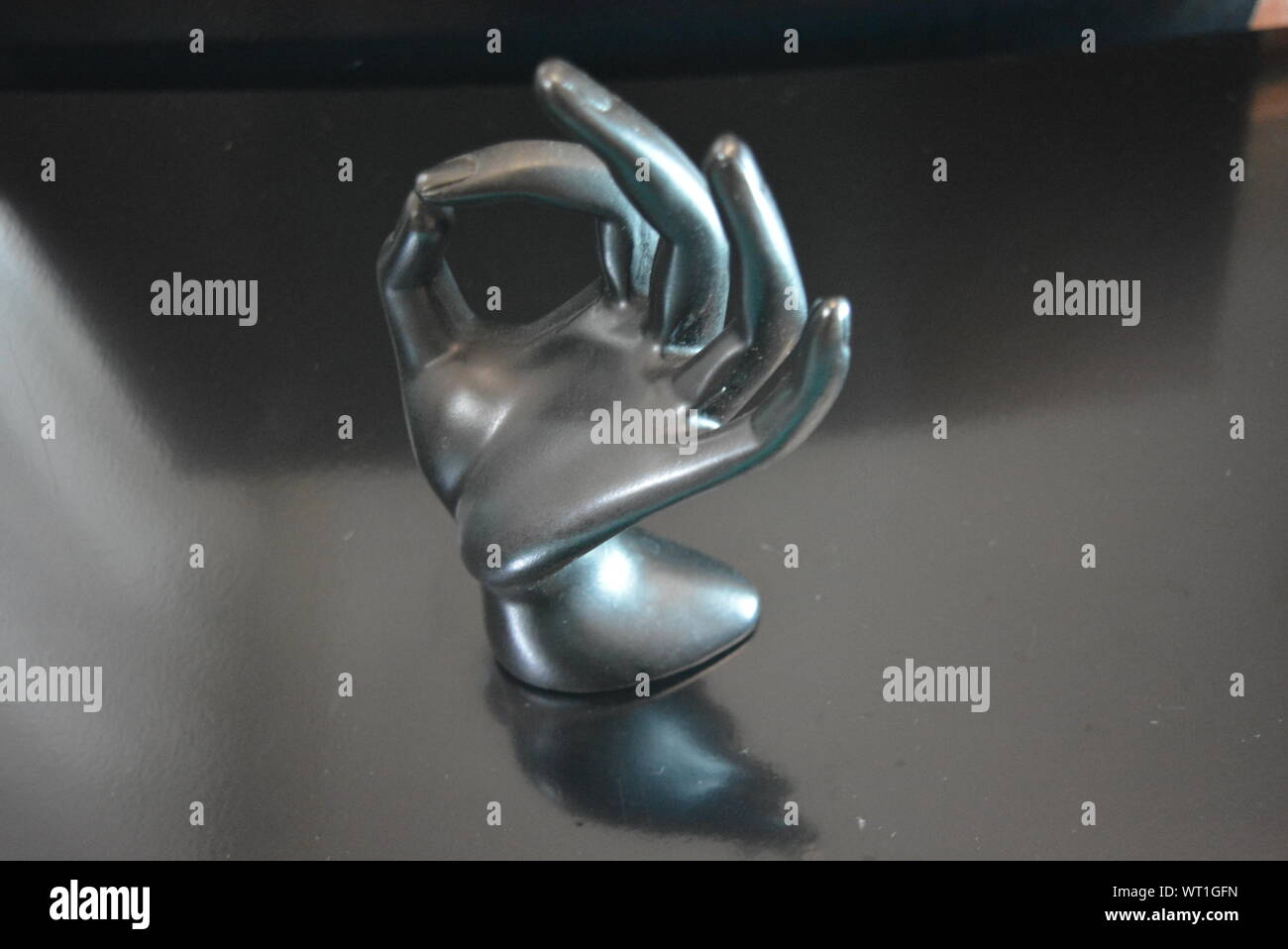 A matte black ceramic hand-shaped statuette is located on a matte black ...