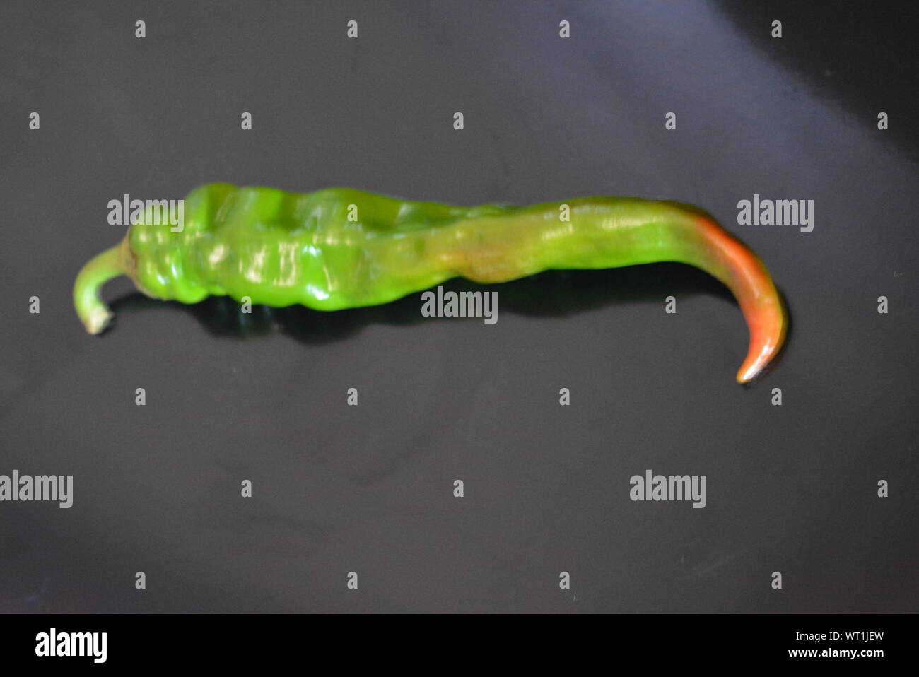 Fresh juicy green bitter peppers, two chili peppers lying on a black ...