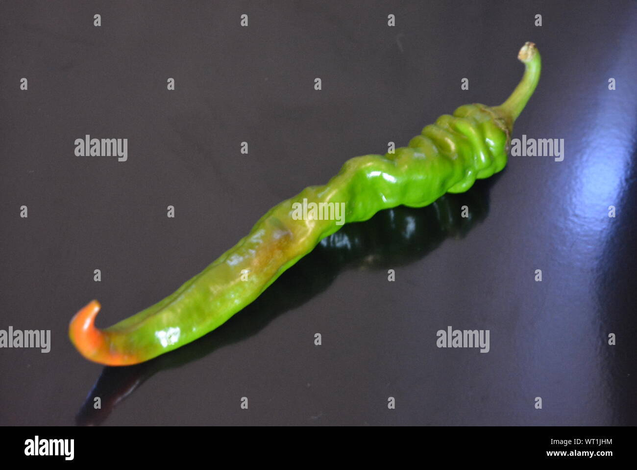 Fresh juicy green bitter peppers, two chili peppers lying on a black ...