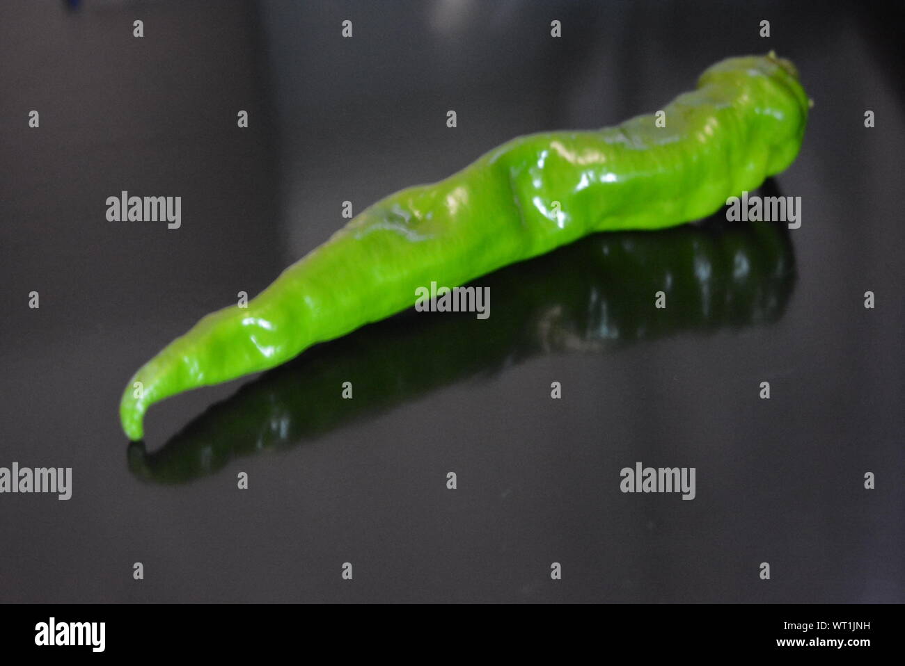 Fresh juicy green bitter peppers, two chili peppers lying on a black ...