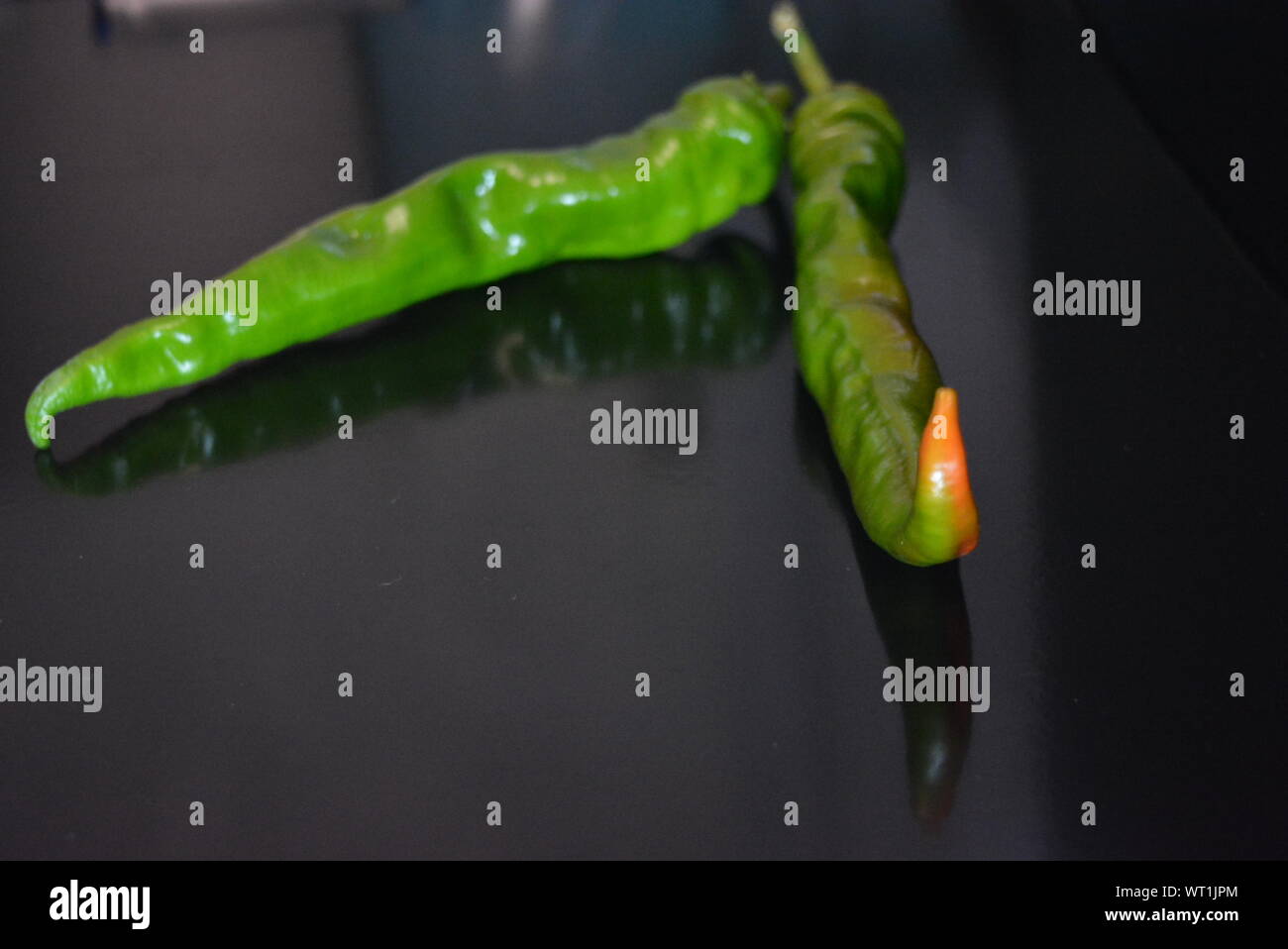 Fresh juicy green bitter peppers, two chili peppers lying on a black ...