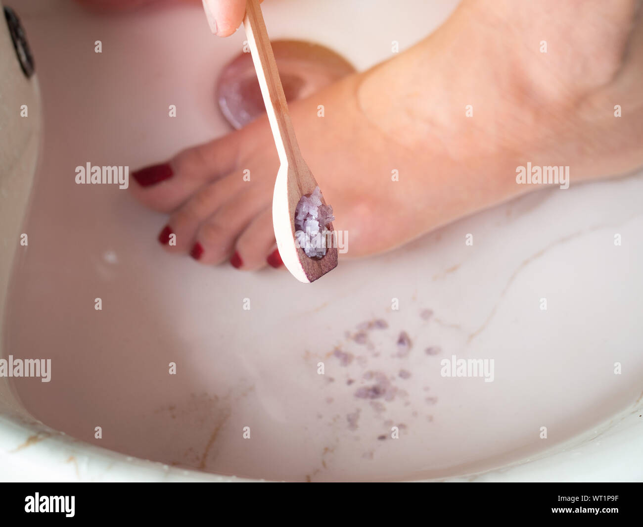 Hand pouring epsom salt from small wooden spoon and female feet in foot ...