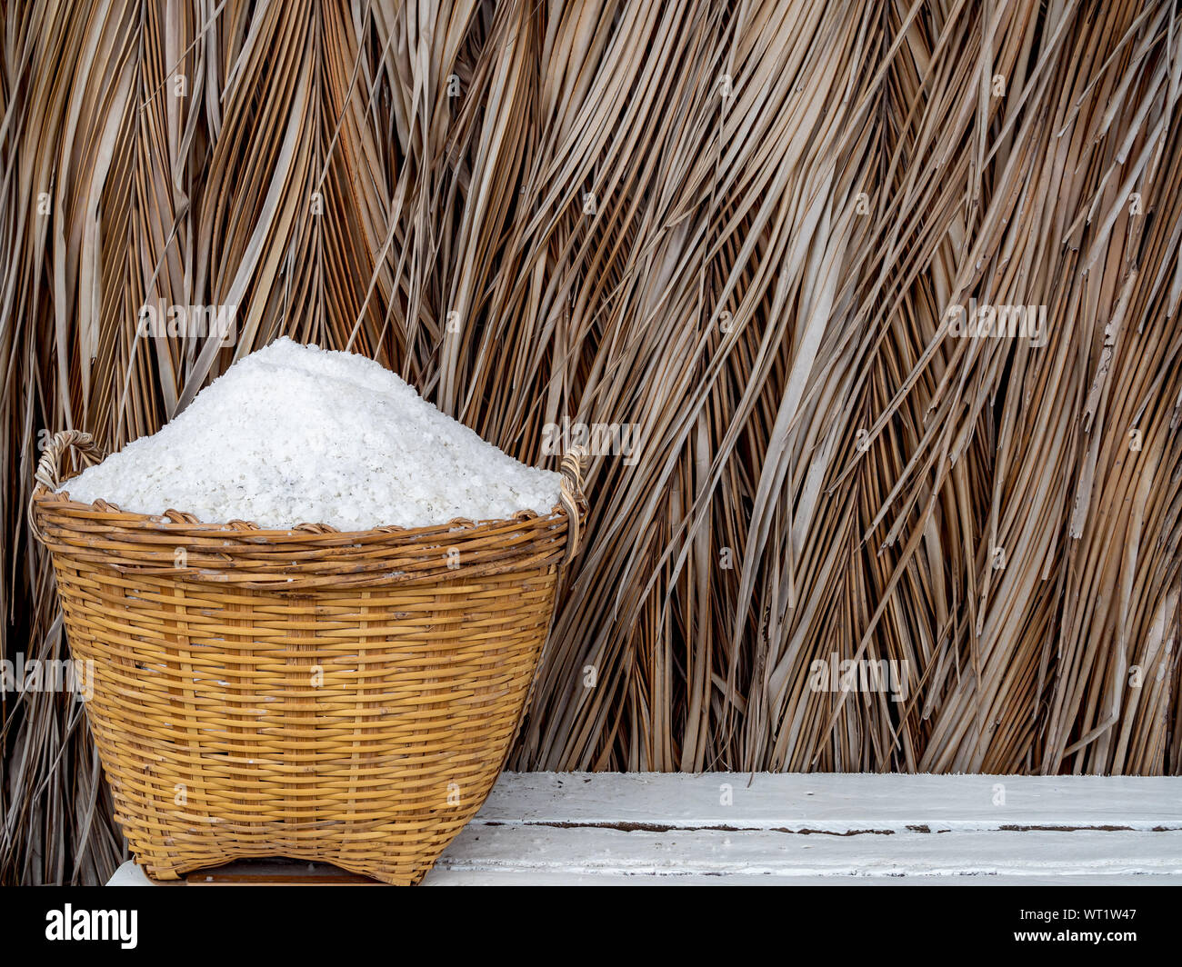 White sea salt in yellow basket on dried tropical palm leaves ...
