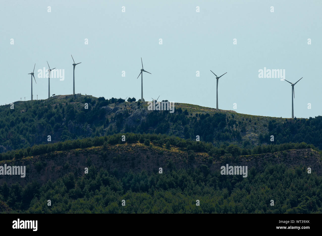 Six wind turbines on top of a forested mountain in a haze against a ...