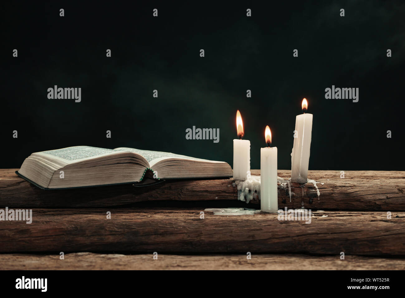 Beautiful open bible and burned candles on a old oak wooden table ...