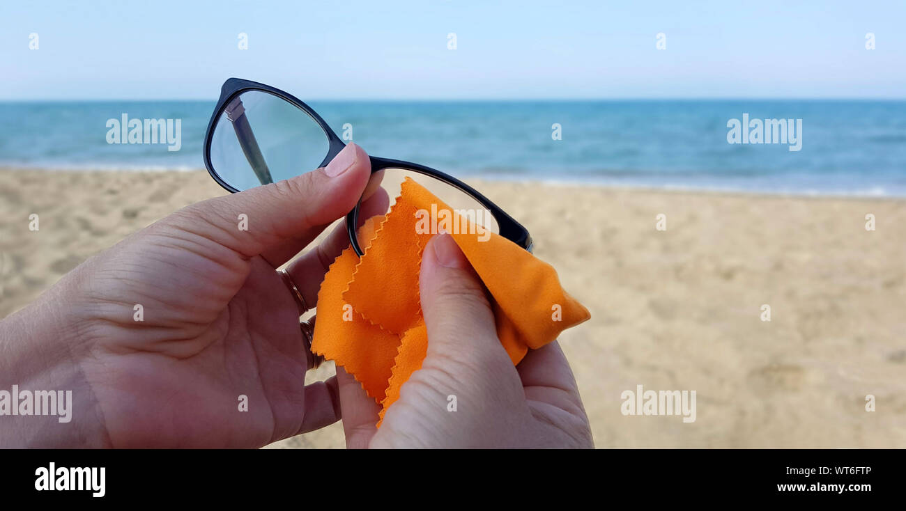 Closeup of hands cleaning glasses lens with orange cloth lens on the ...