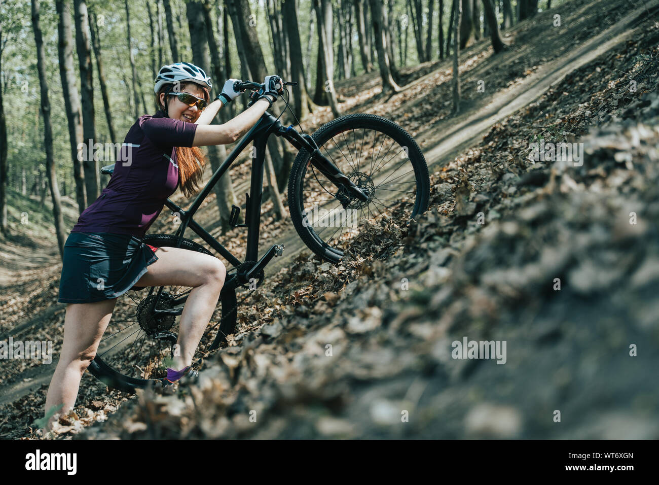 Photo on side of female athlete in helmet raising bicycle to hill in ...