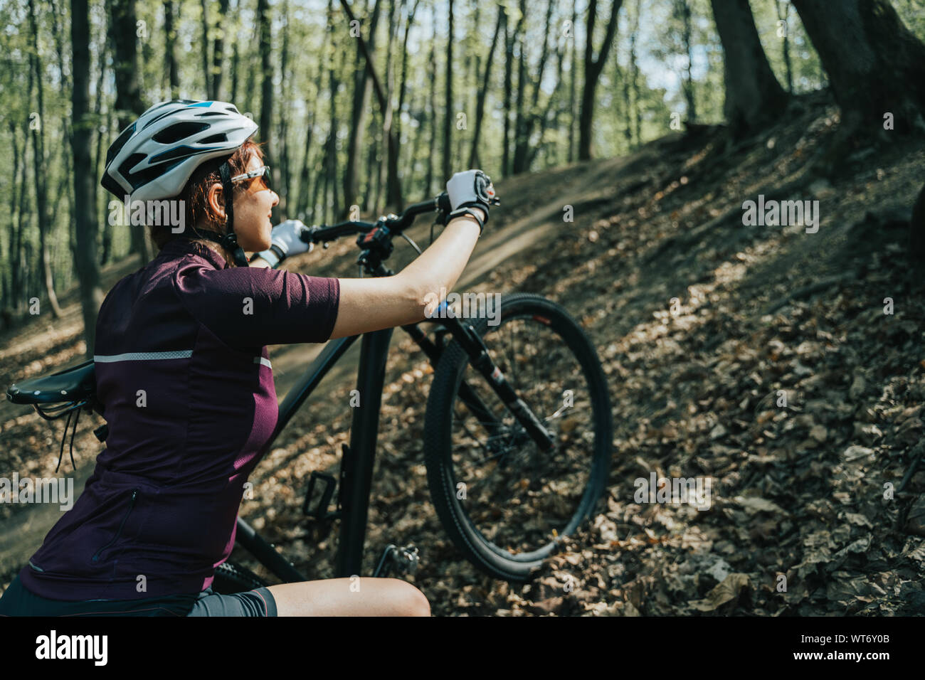 Photo of athlete woman in helmet raising bicycle to hill in forest on ...