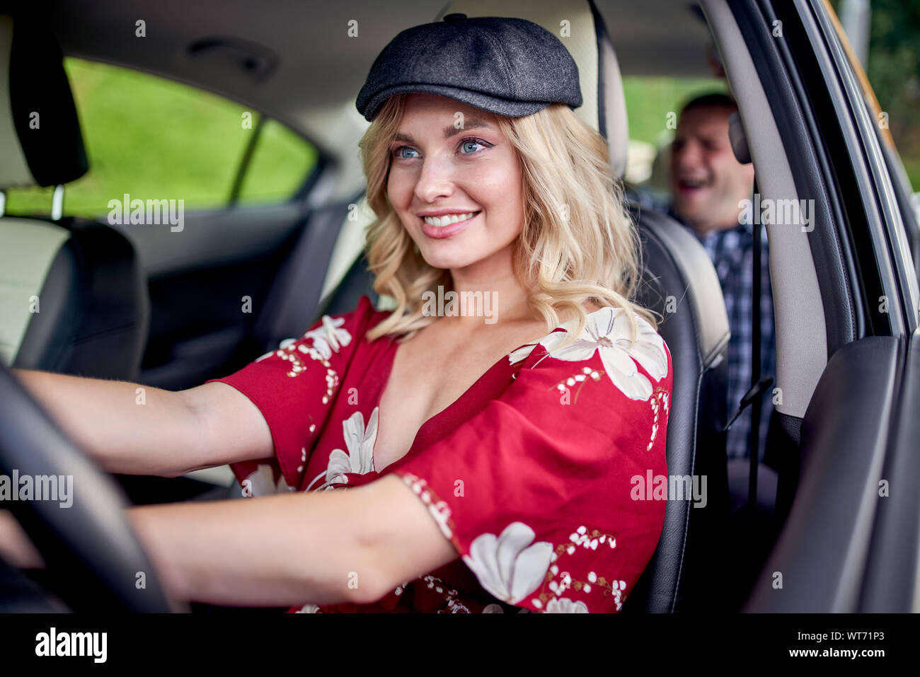 Image of happy blonde female driver driving, male passenger in car ...