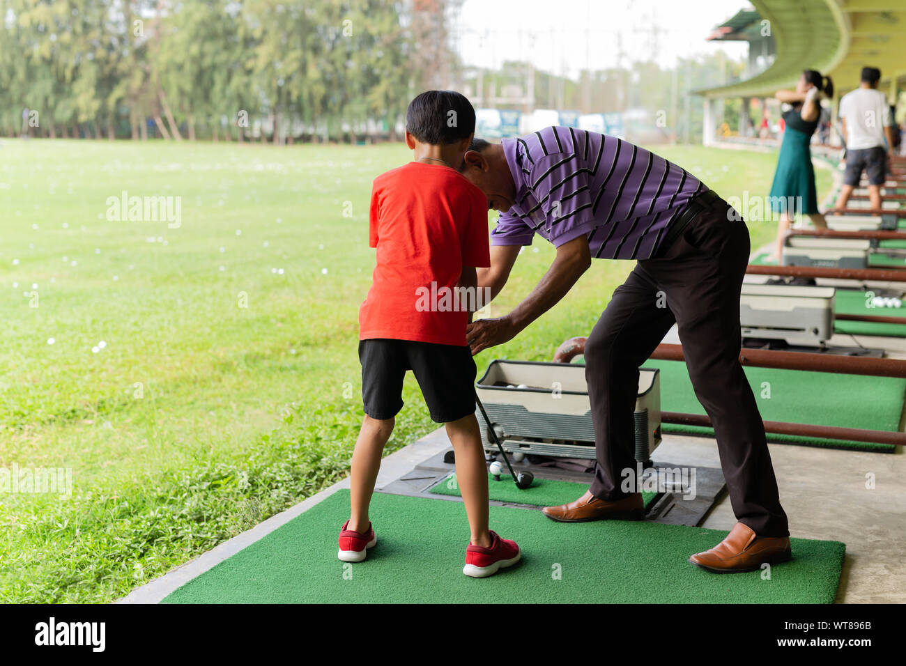 Personal trainer giving lesson to young boy in golf driving range Stock ...