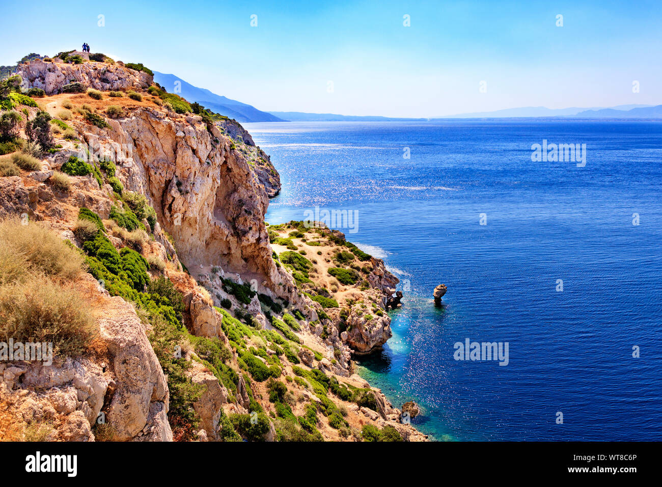 Calm turquoise waves wash the rocky shore of the Gulf of Corinth in the ...