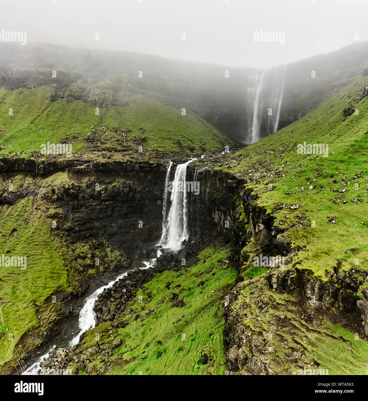 Thick mist floating over green mossy slope and cool waterfall on dull ...