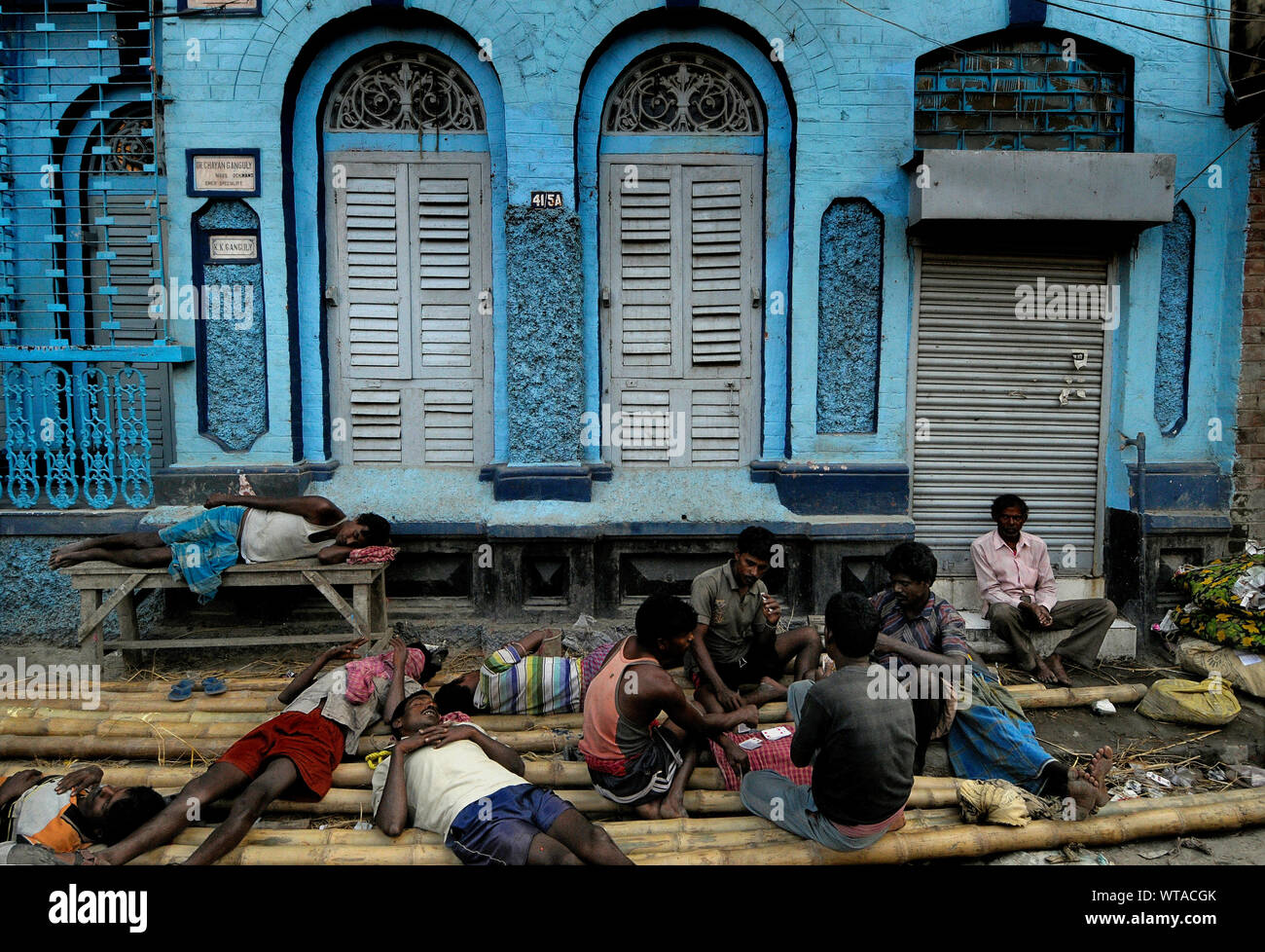 Labourers sleep in a street outside a house painted in blue colour in ...