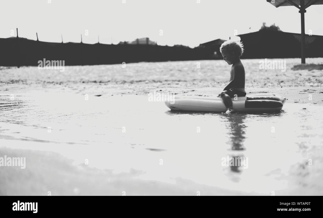 Boy Sitting On Inflatable Raft Against Sea At Beach Stock Photo - Alamy
